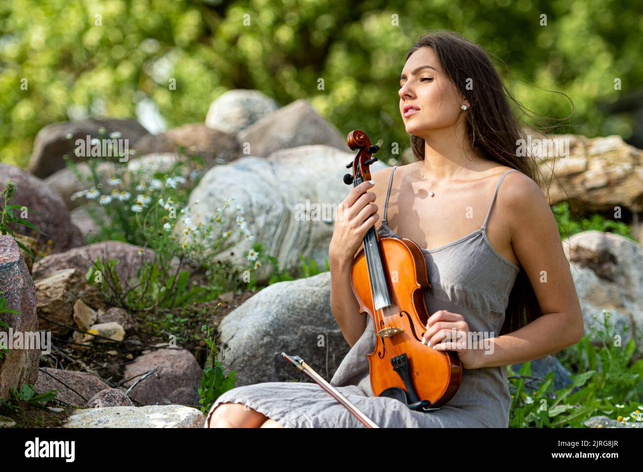 beautiful brunette in a linen dress with a violin on a pile of boulders ...