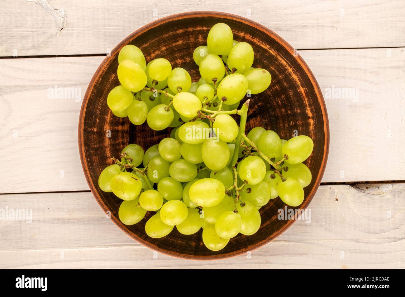 One bunch of white grapes with a ceramic plate on a wooden table, close ...