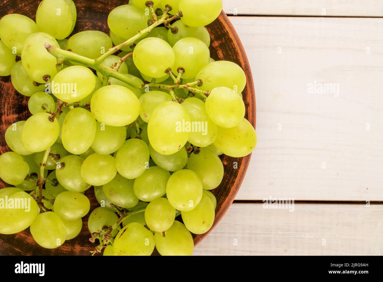 One bunch of white grapes with a ceramic plate on a wooden table, close ...