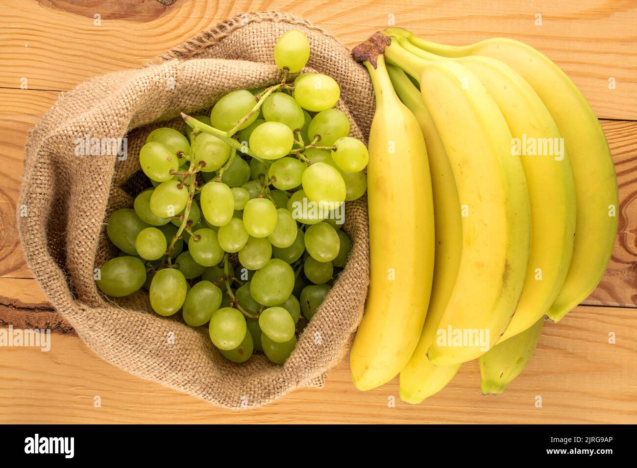 One bunch of white grapes and bananas with a jute bag on a wooden table ...