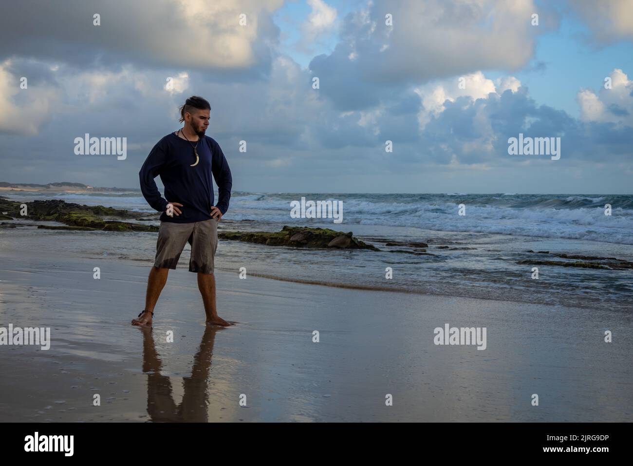Middle-aged bearded man on the beach during sunrise looking lost at the ...
