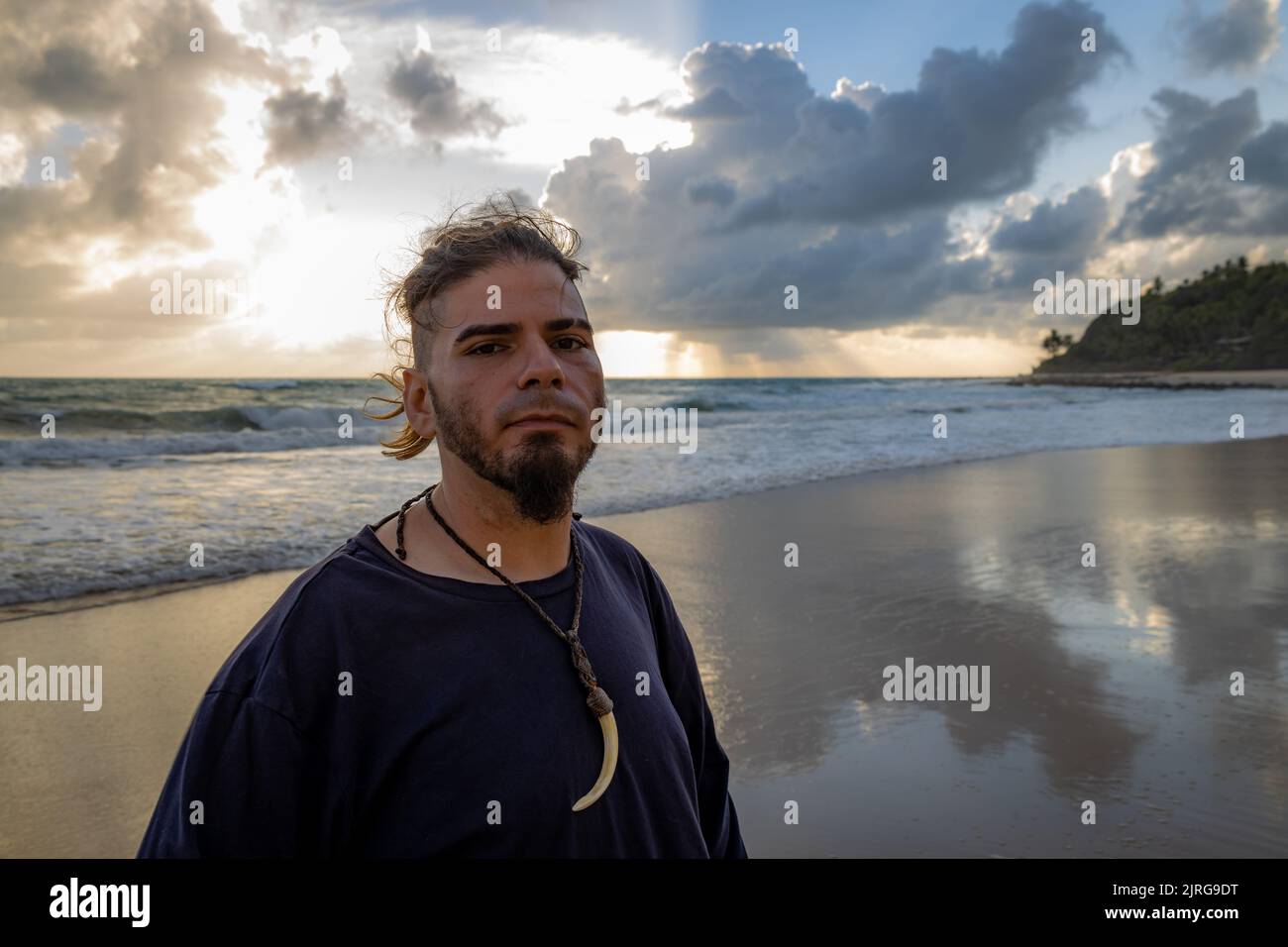 Middle-aged bearded man on the beach during sunrise with defiant look ...