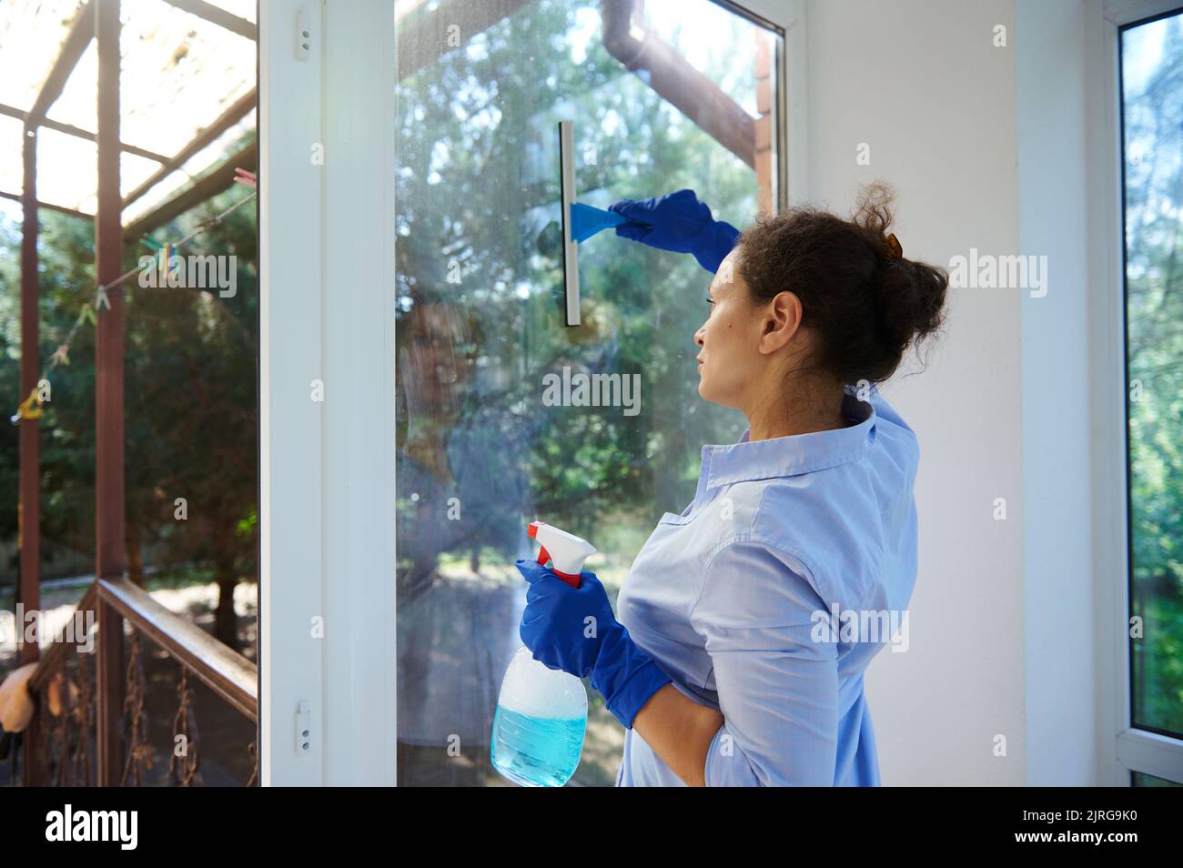 Rear view of a maid doing household chores cleaning windows, removing ...