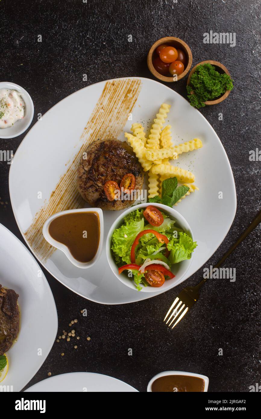 Grilled beef steaks with potato, vegie and steak sauce at white plate ...