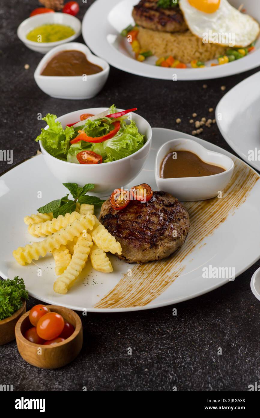Grilled beef steaks with potato, vegie and steak sauce at white plate on texture rustic table ...