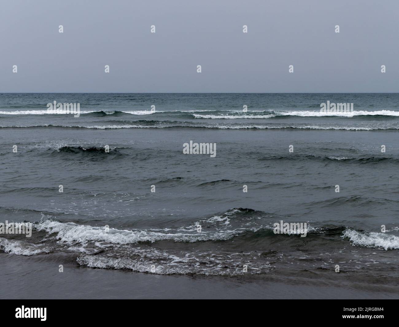 Waves on the sea surface on a cold cloudy day. The horizon line over ...