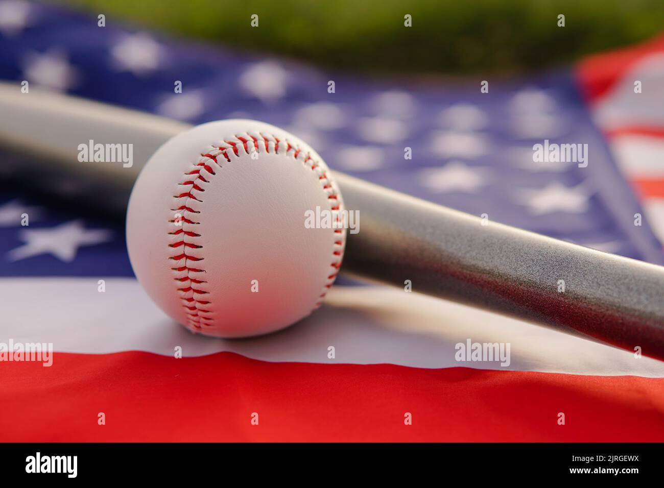 White leather ball and baseball bat laying on flag of the United States ...