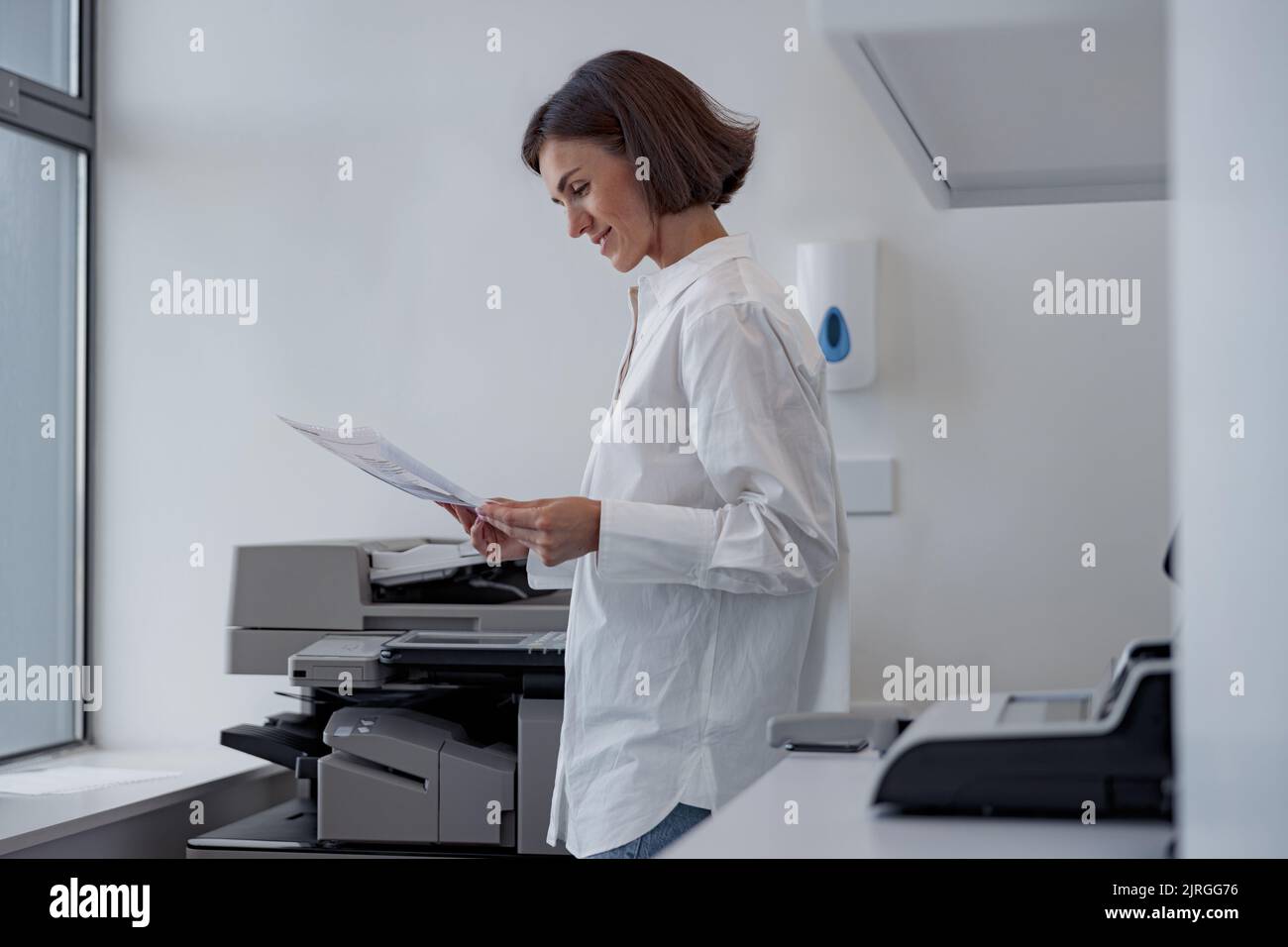 Smiling woman worker scanning a document on photocopy machine In modern ...