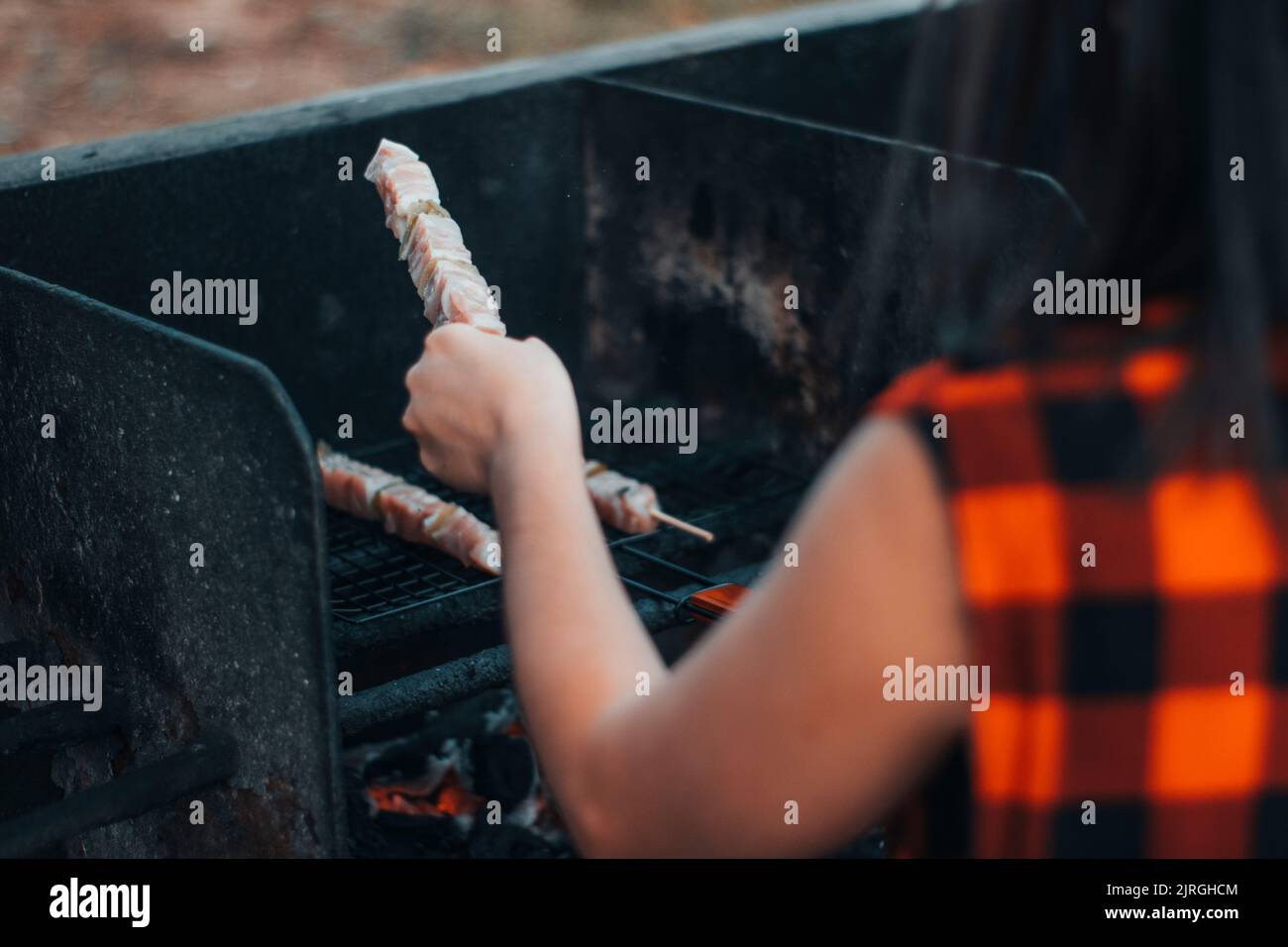 A closeup view of a Spanish girl cooking meat on a grill mesh in a park ...