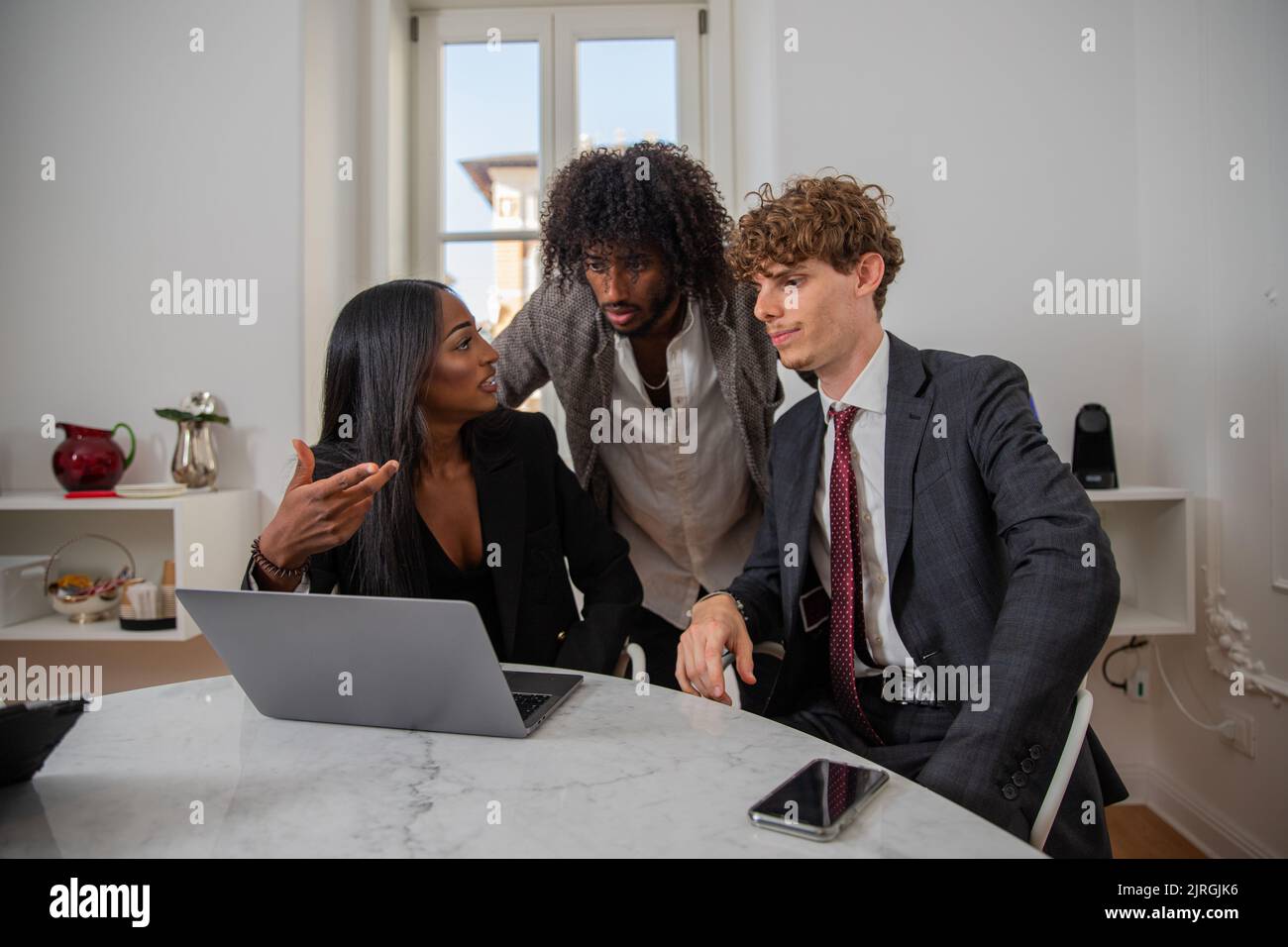 Colleagues discuss at work using a laptop, multi-ethnic business group ...
