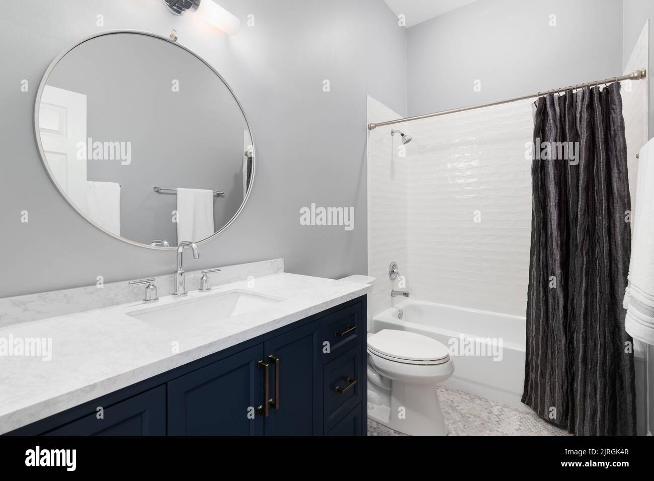 An elegant bathroom with a blue vanity cabinet, circular mirror, subway ...