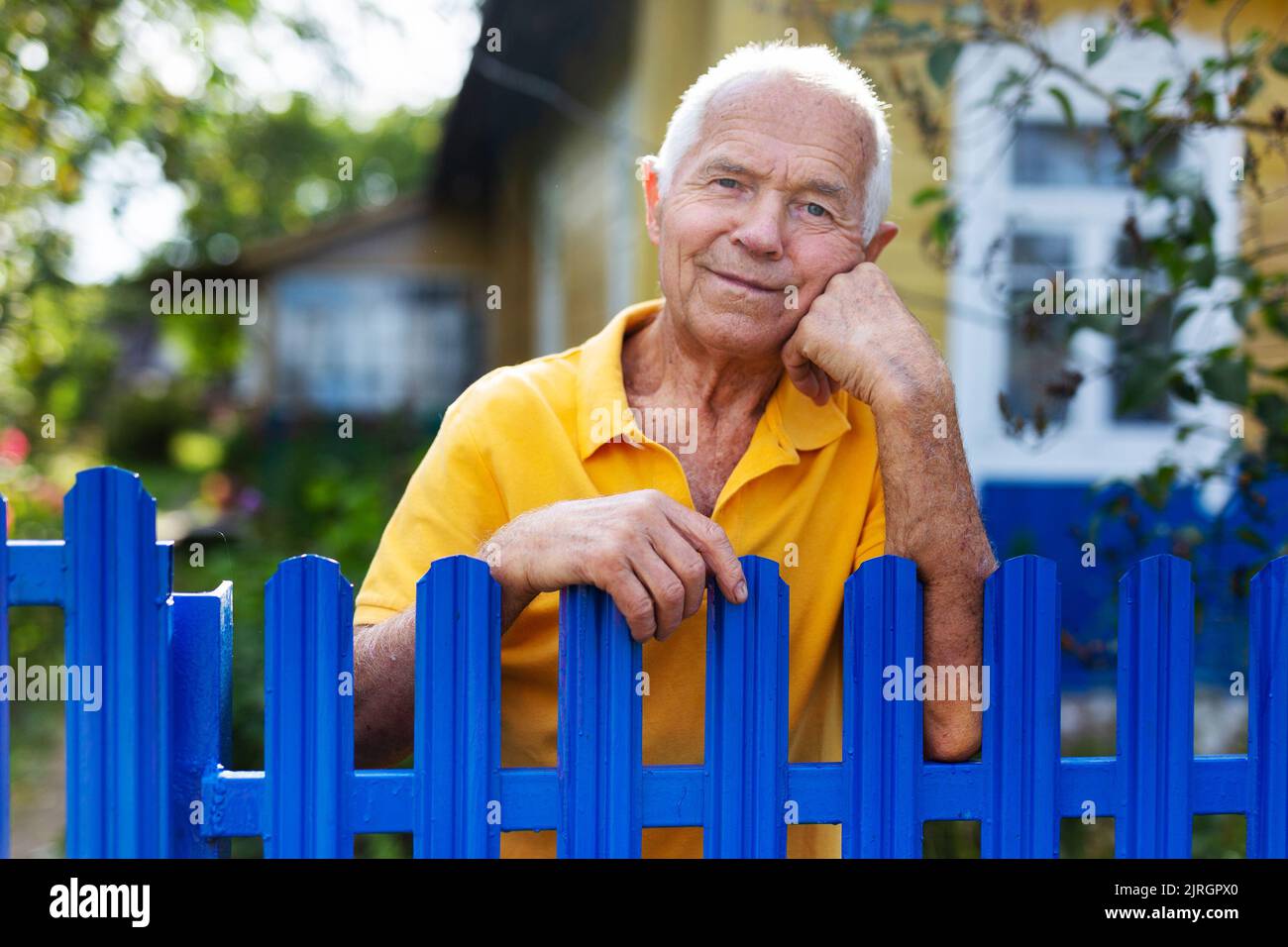 Portrait of pensive elderly man at fence of his country house in ...