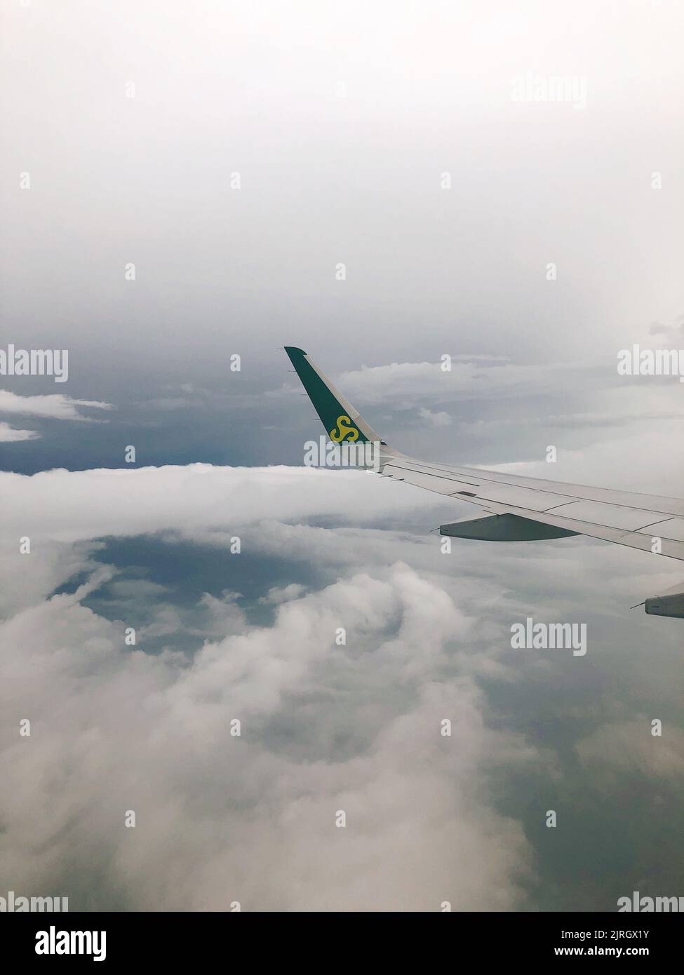 A vertical shot of a Spring Airlines airplane flying in the clouds in ...