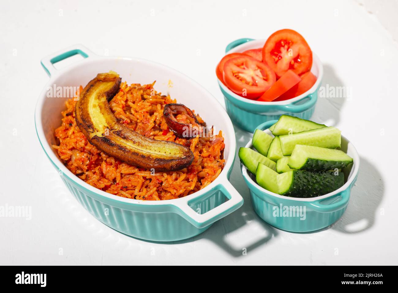 Jollof rice with fried banana. Fresh vegetables - tomato and cucumber ...