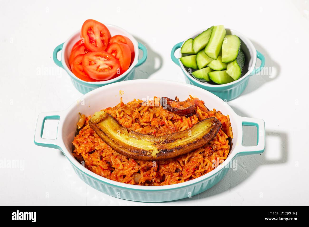 Jollof rice with fried banana. Fresh vegetables - tomato and cucumber ...