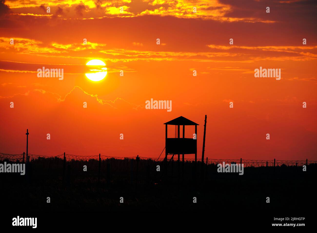 Fence with barbed wire and an old watchtower background bright sun and ...