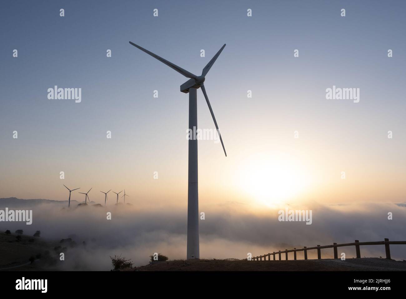 Wind turbines in the fog. Wind farm at sunset and sun above the clouds ...