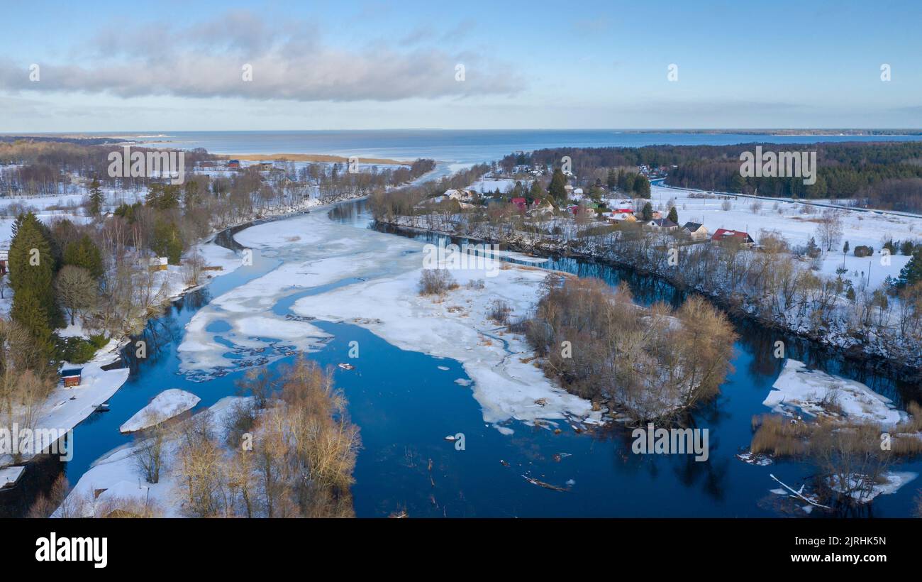 An aerial view of a frozen river with shoreline buildings in winter ...