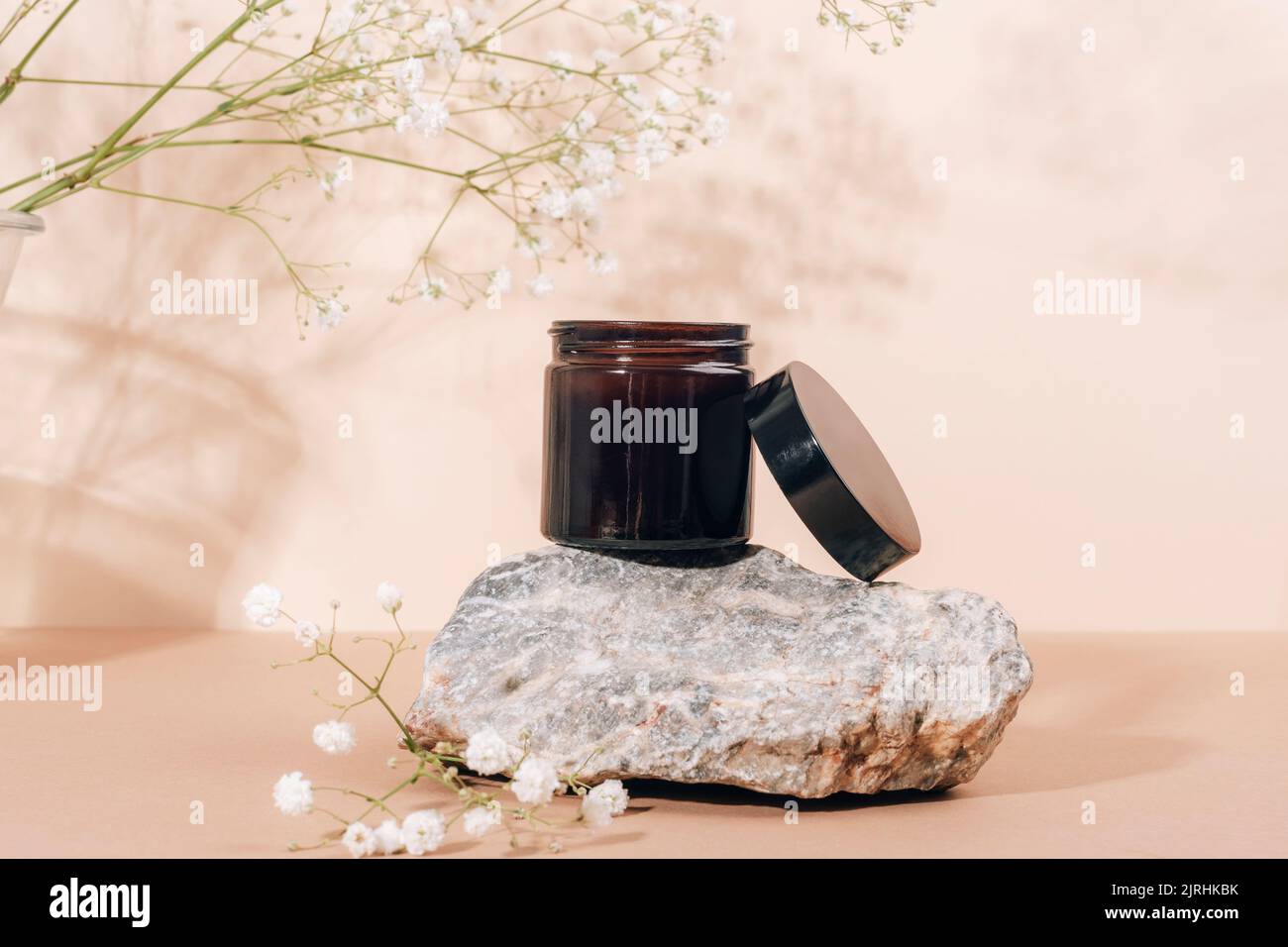Cream in brown glass jar on natural stone with gypsophila flowers in ...