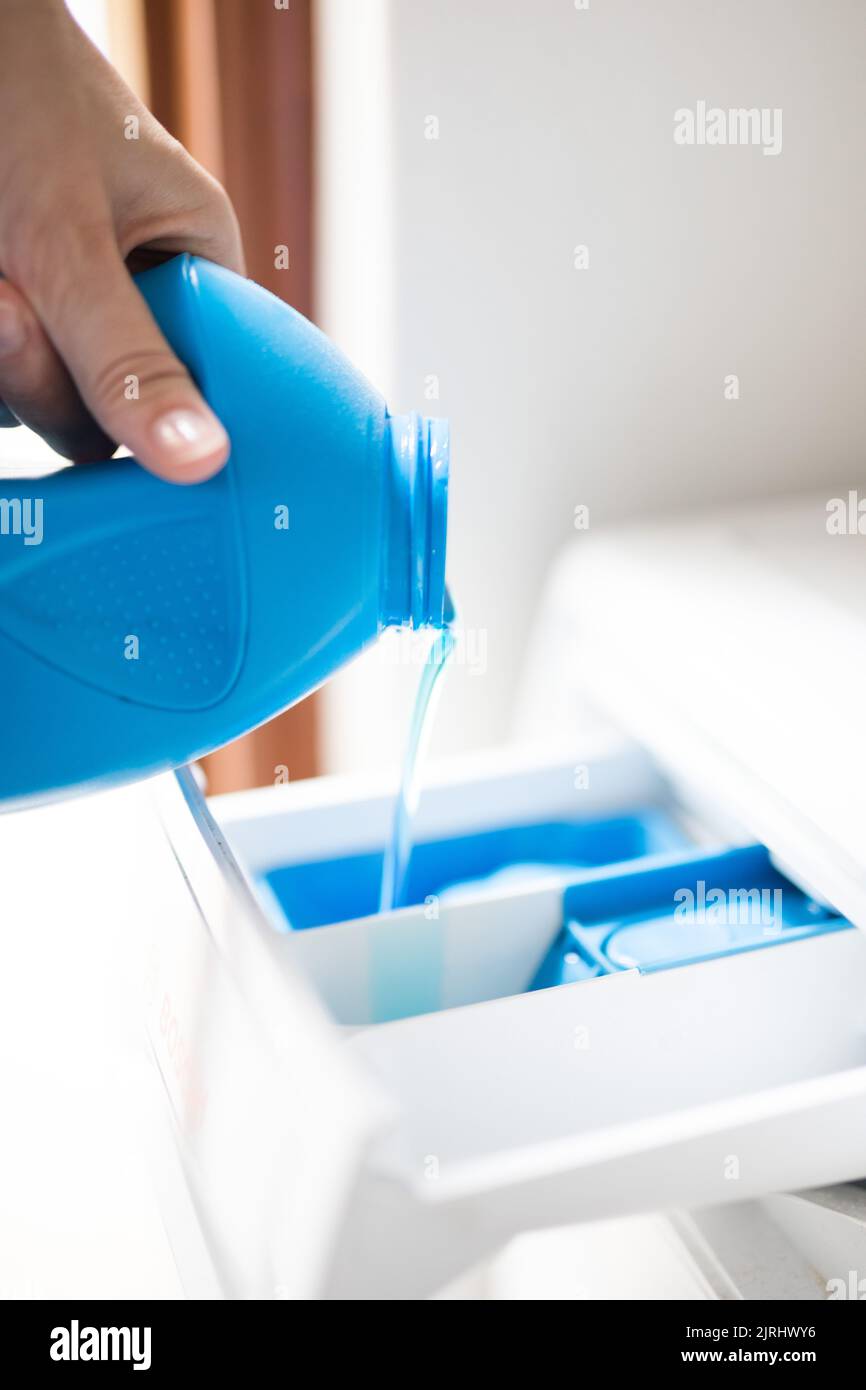 A female hand pouring a blue liquid detergent into a washing machine ...