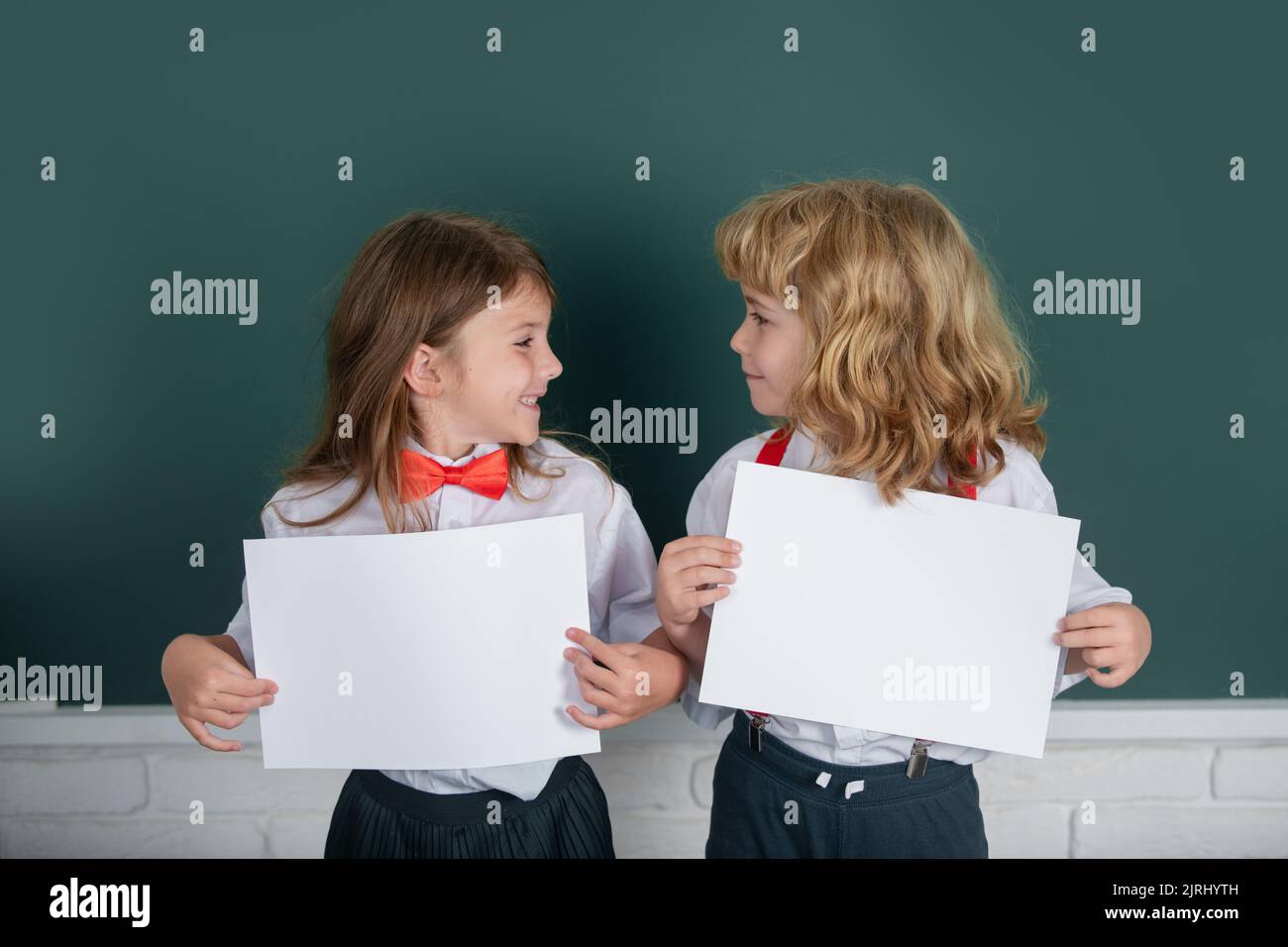 Two schoolkids holding white paper blank, poster with copy space ...