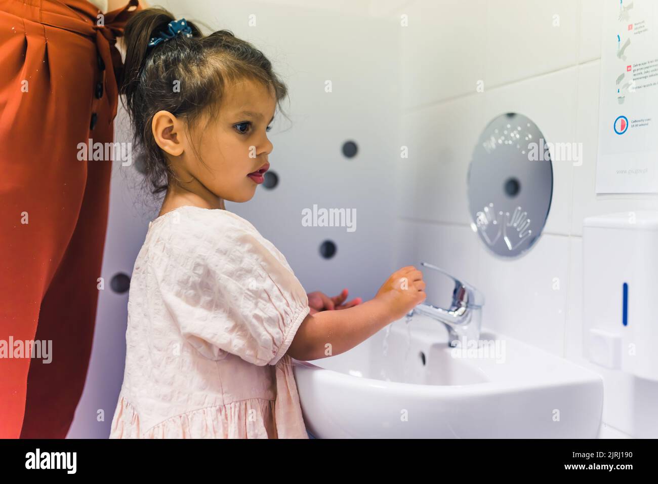 Toddler girl washing her hands with soap after playtime at the nursery ...