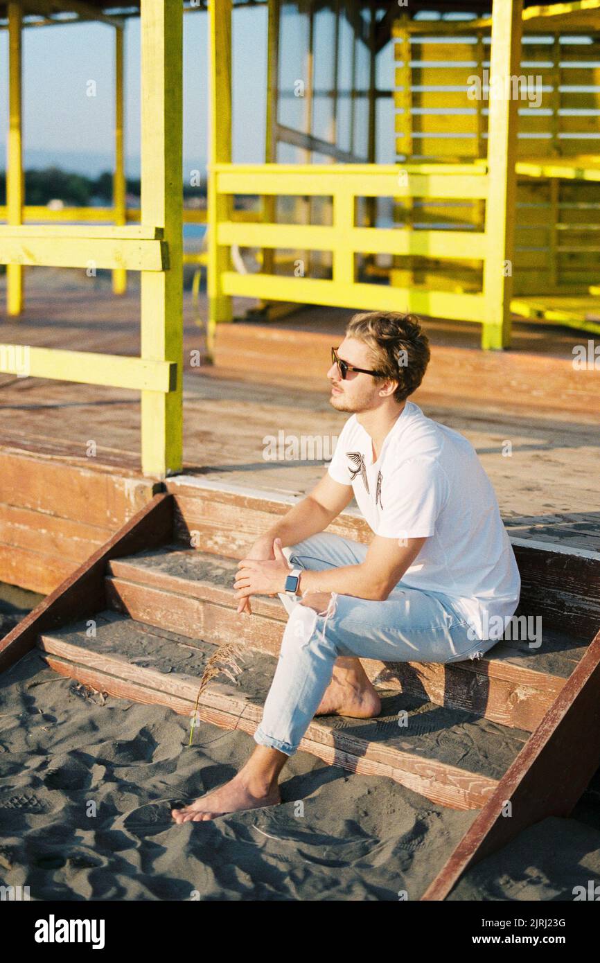 Young man in sunglasses sitting on the steps of a wooden building on ...