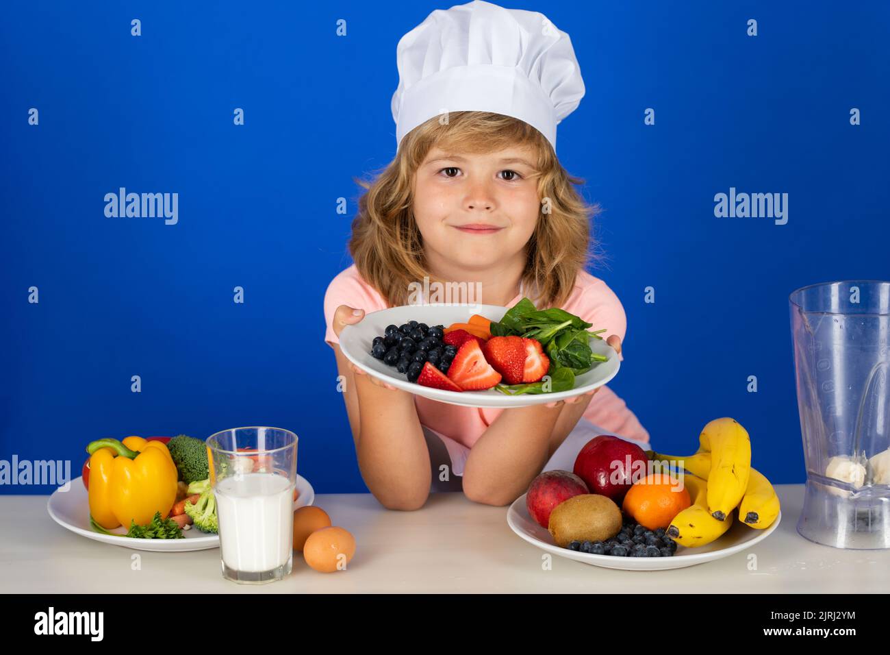 Child chef cook hold plate with fruits prepares food in isolated blue ...