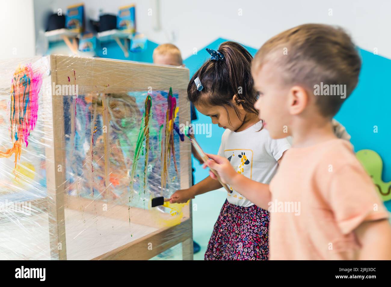 Cling film painting. Toddler painting with a sponge, brushes and paints ...