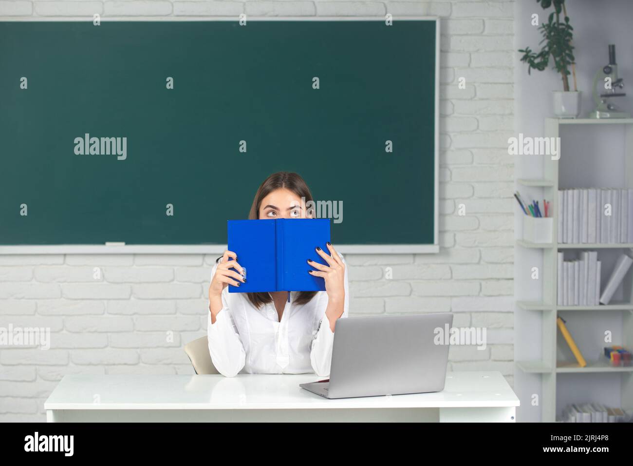 Female college student hiding behind an open book and looking away ...