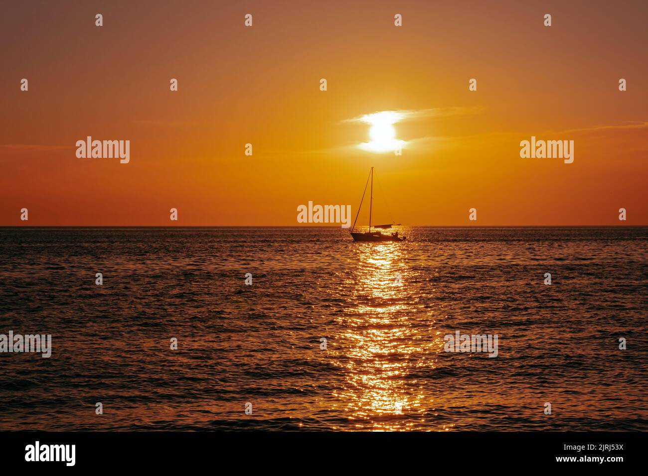 A beautiful sunset over the ocean with yellow sky and a boat sailing on ...