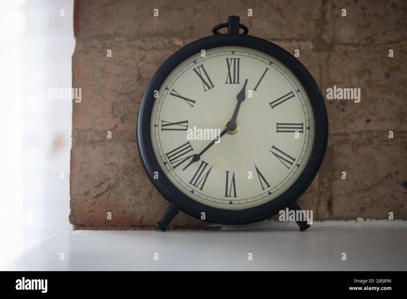 A closeup shot of a round clock with roman numerals on a white shelf on ...