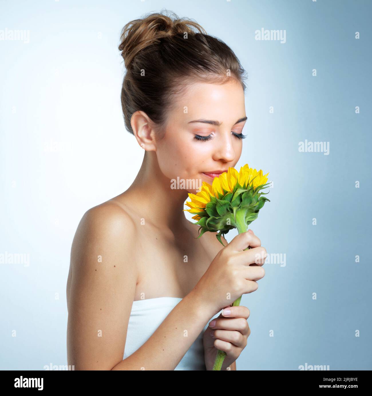 Shes a delicate beauty. Studio shot of a beautiful young woman smelling a sunflower Stock Photo ...