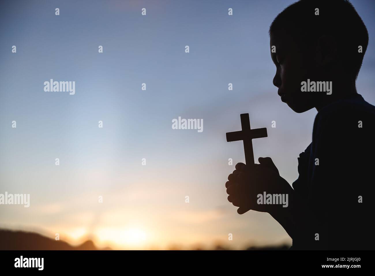 Silhouette of child praying with cross in nature sunrise background ...
