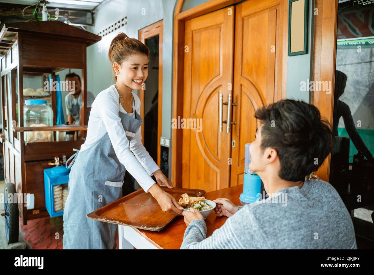 the waiter serves chicken noodle dish to male customers Stock Photo - Alamy