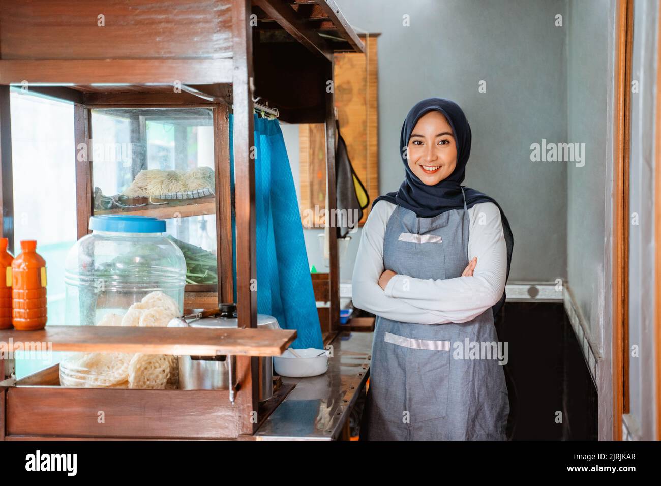 hijab woman wearing apron smiling while standing with crossed hands ...