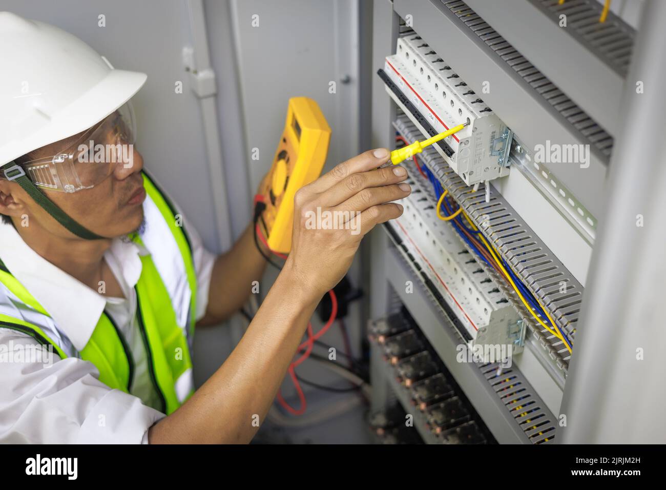 A male electrician works in a control panel with electrical connections ...