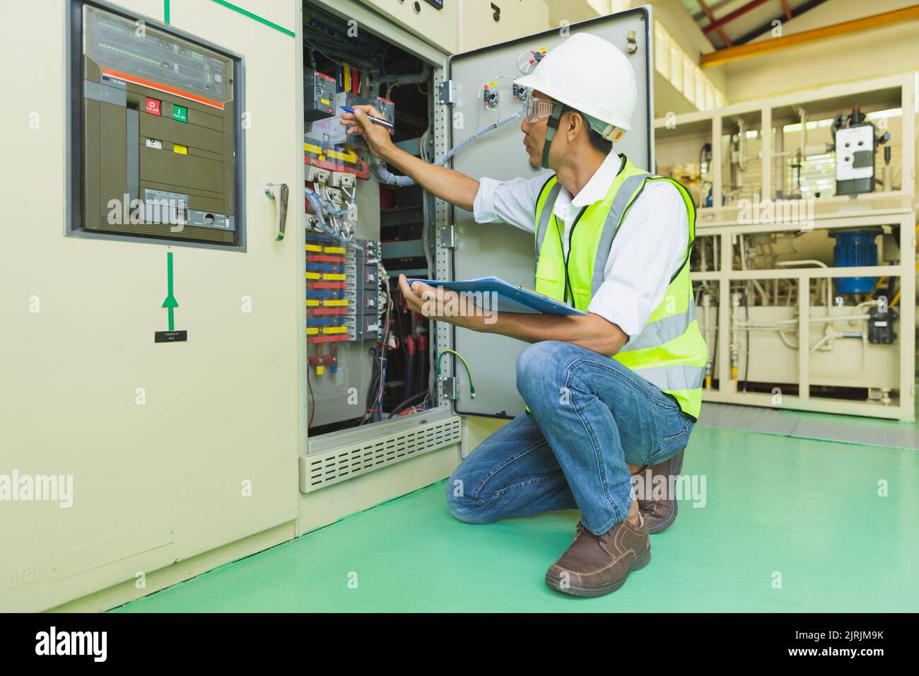 A helmeted technician holds a clipboard while checking and taking notes ...