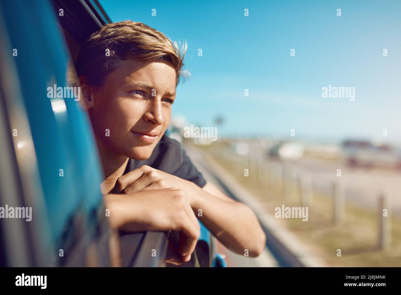 Life is a highway. a happy young boy leaning out of the car window on a ...
