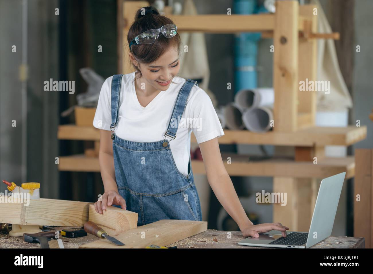 A carpenter woman works in her own woodworking shop. She uses a tablet ...