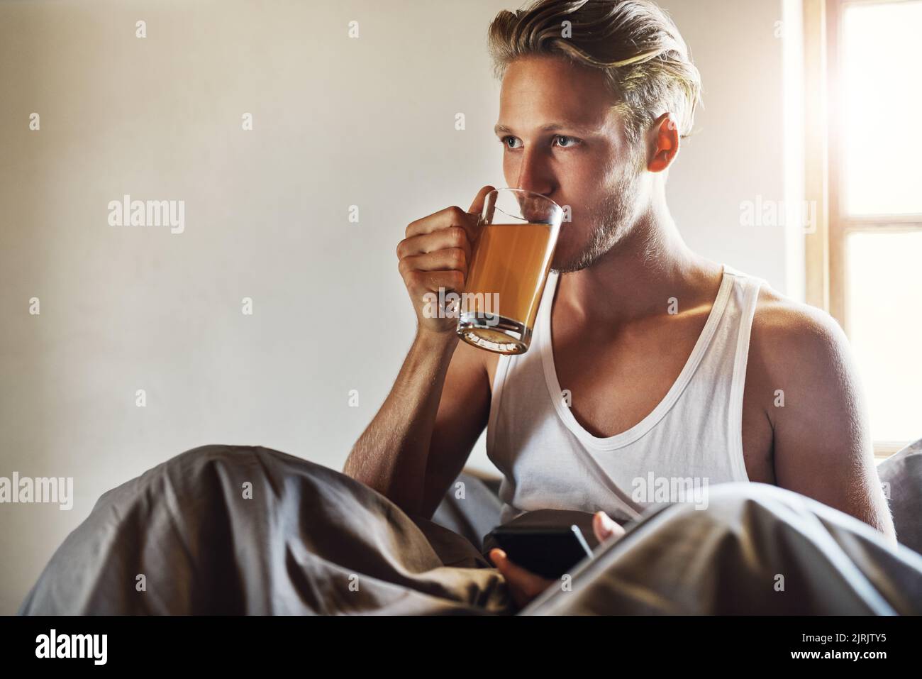 Tea time in bed. a handsome young man using his cellphone while ...