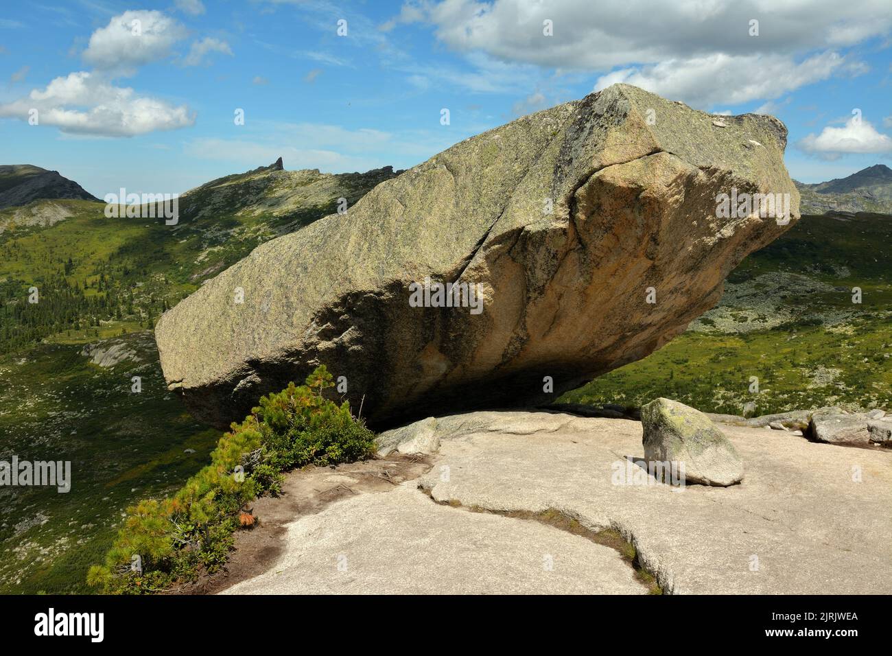 A huge granite monolith hangs on the edge of a high cliff overlooking a ...