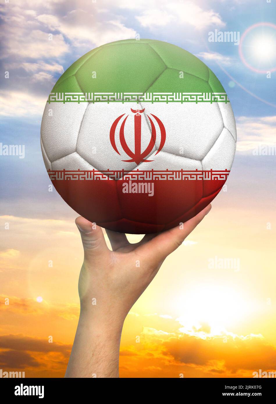Soccer ball in hand with a depiction of the flag of Iran against a ...