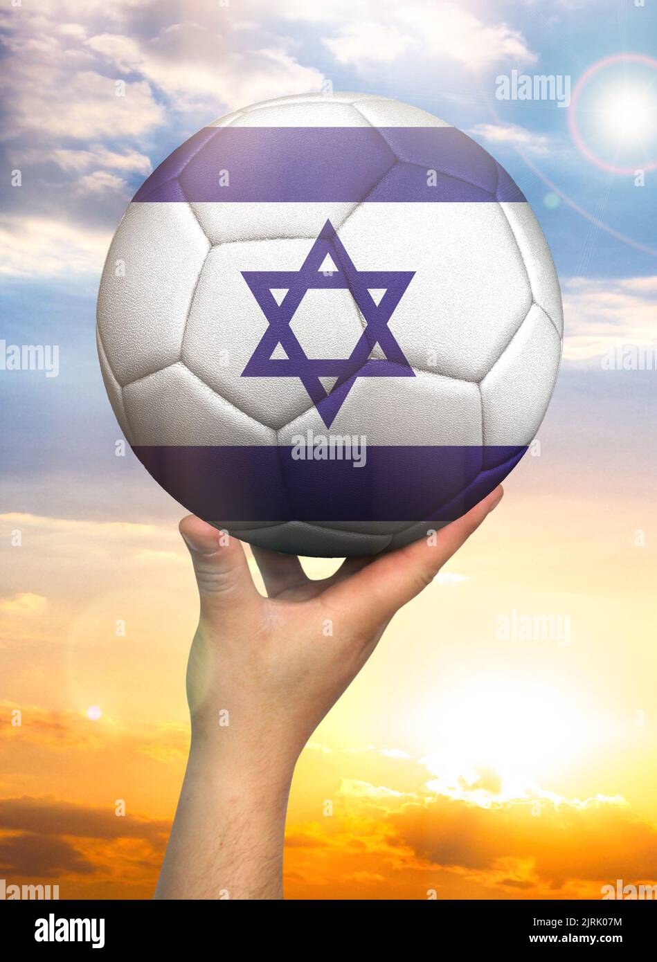 Soccer ball in hand with a depiction of the flag of Israel against a ...