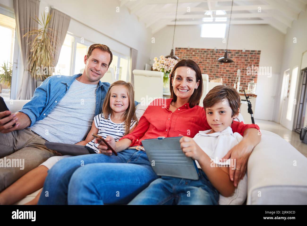 This family loves their devices. Portrait of a smiling family sitting ...