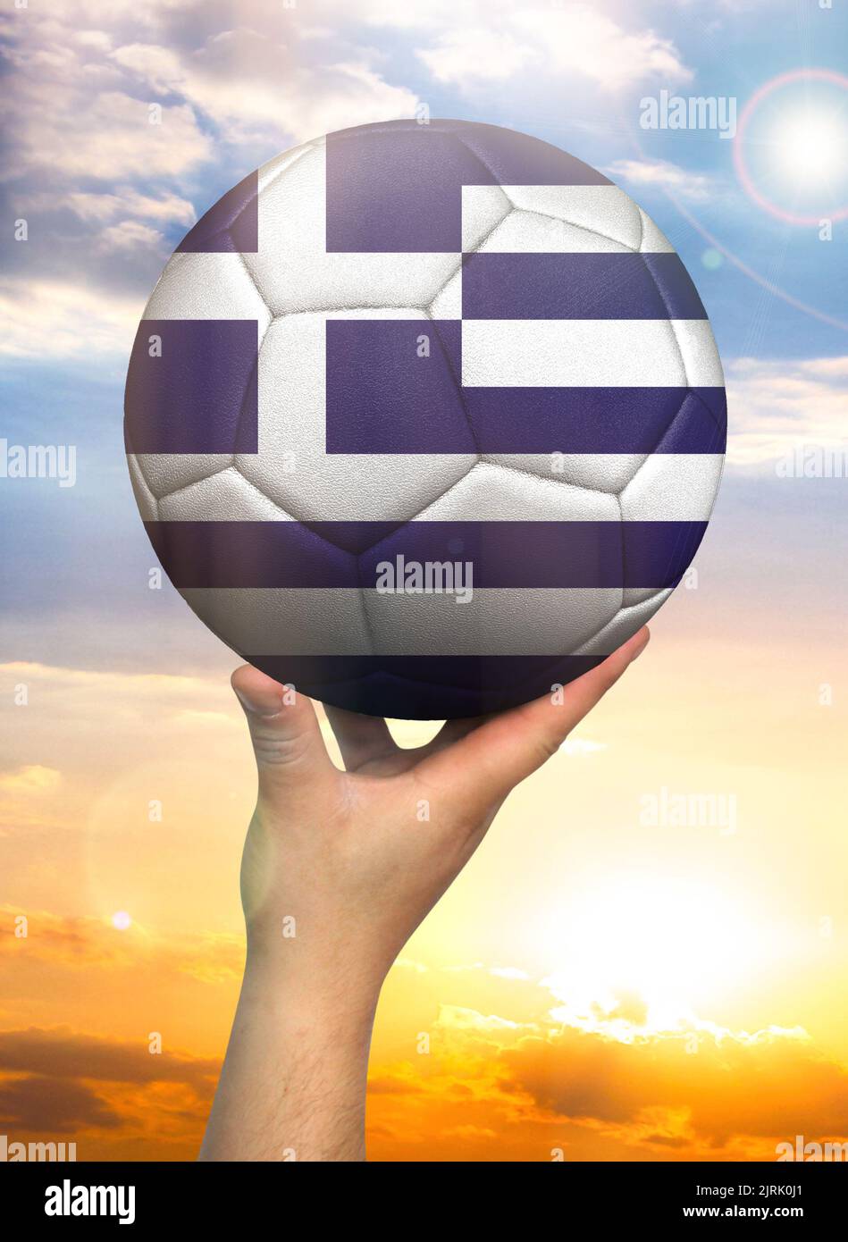 Soccer ball in hand with a depiction of the flag of Greece against a ...
