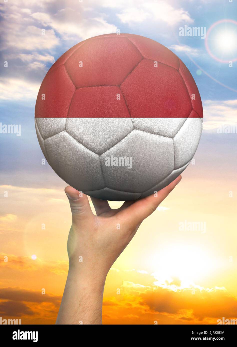 Soccer ball in hand with a depiction of the flag of Indonesia against a ...