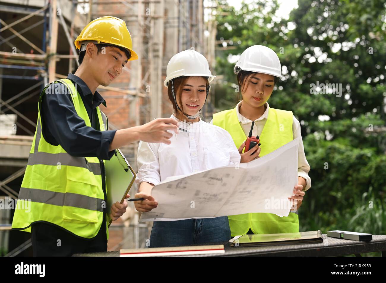 Team of civil engineers and real estate investor wearing safety helmets and vests examining ...