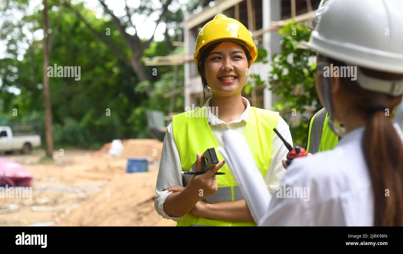 Smiling female engineer supervisor and investor wearing safety helmets ...