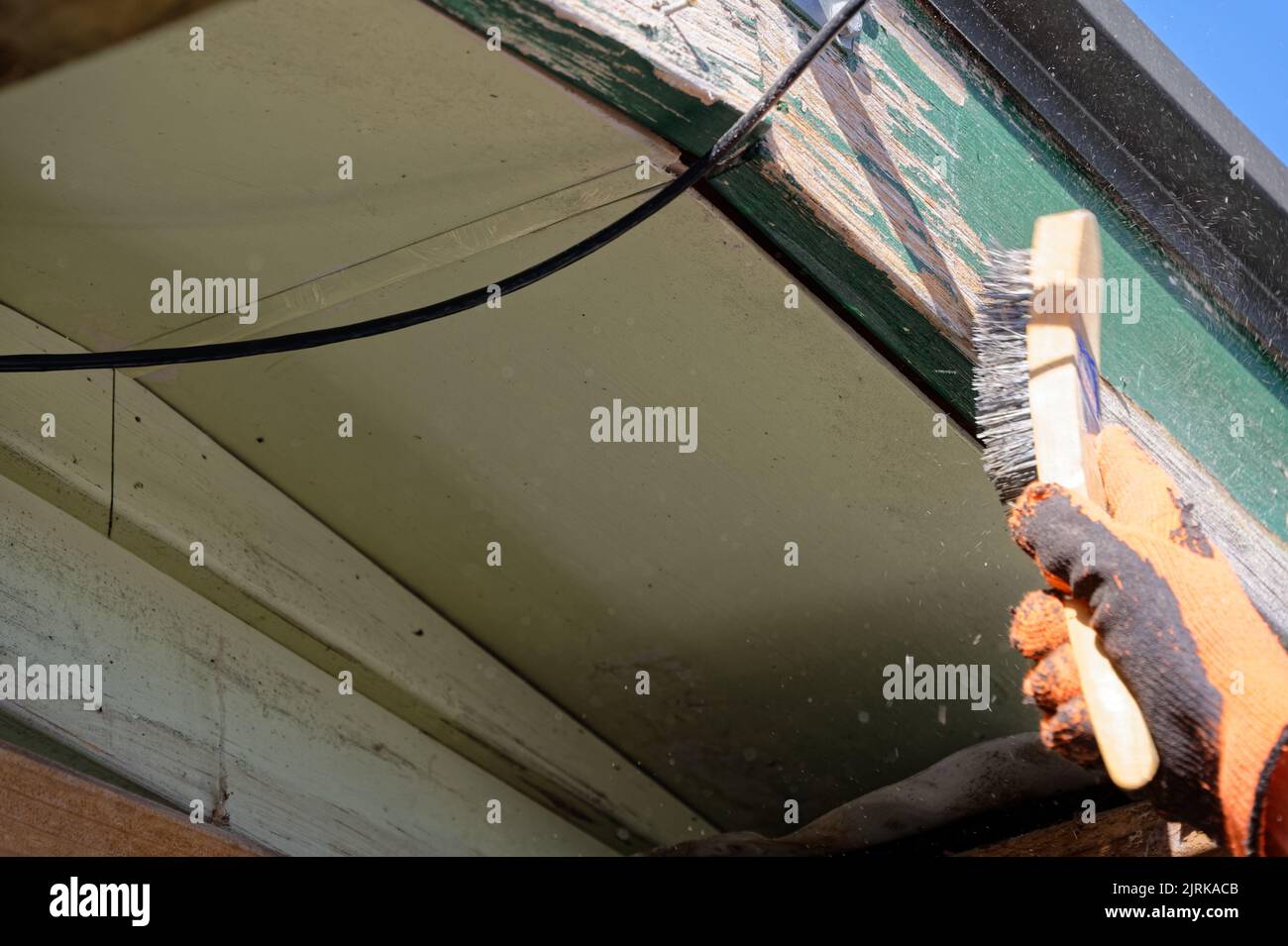 A painter or home handyman is up a ladder with a wire brush taking ...